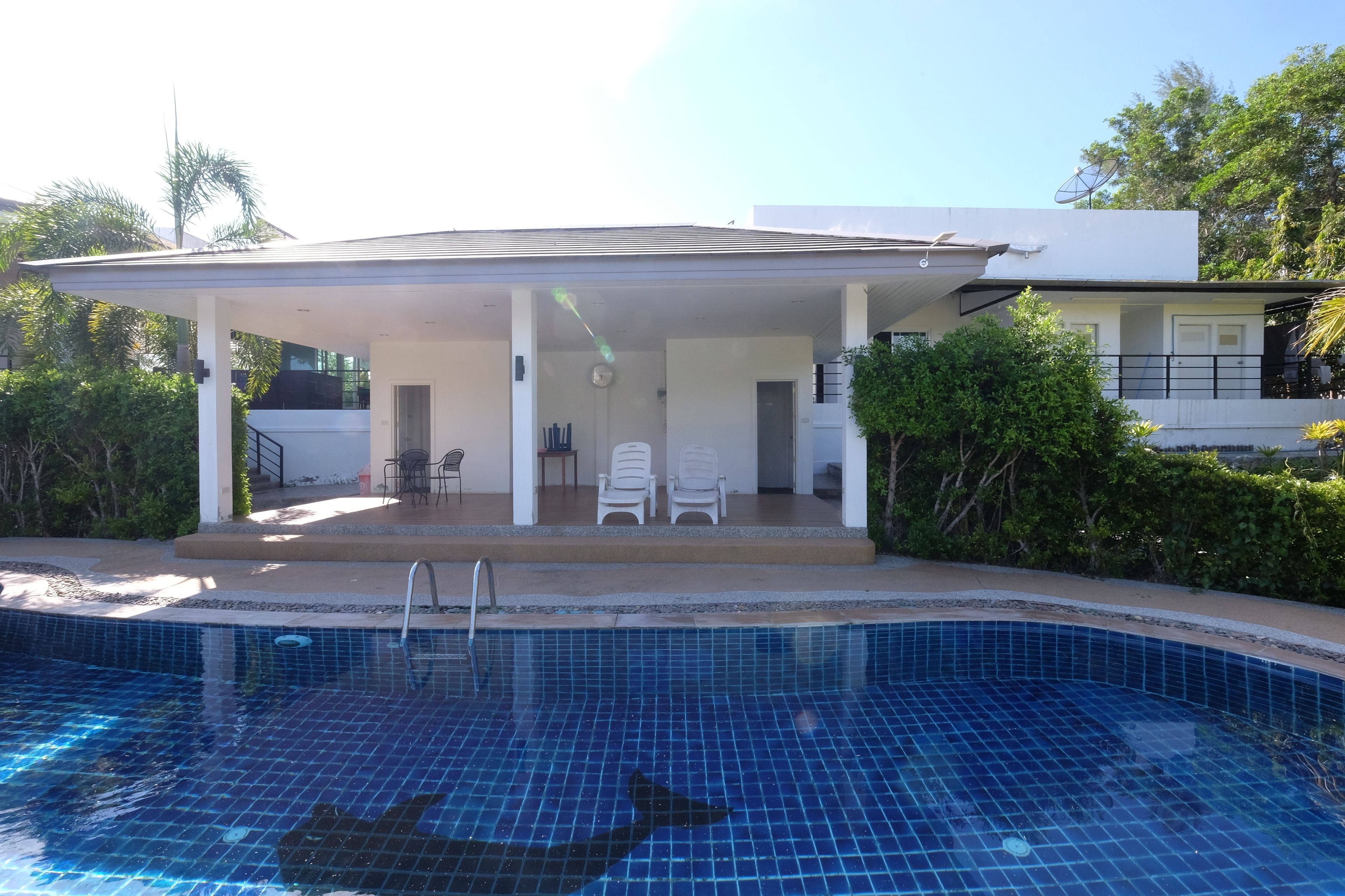 Uma casa moderna com piscina, varanda coberta com cadeiras e vegetação exuberante.