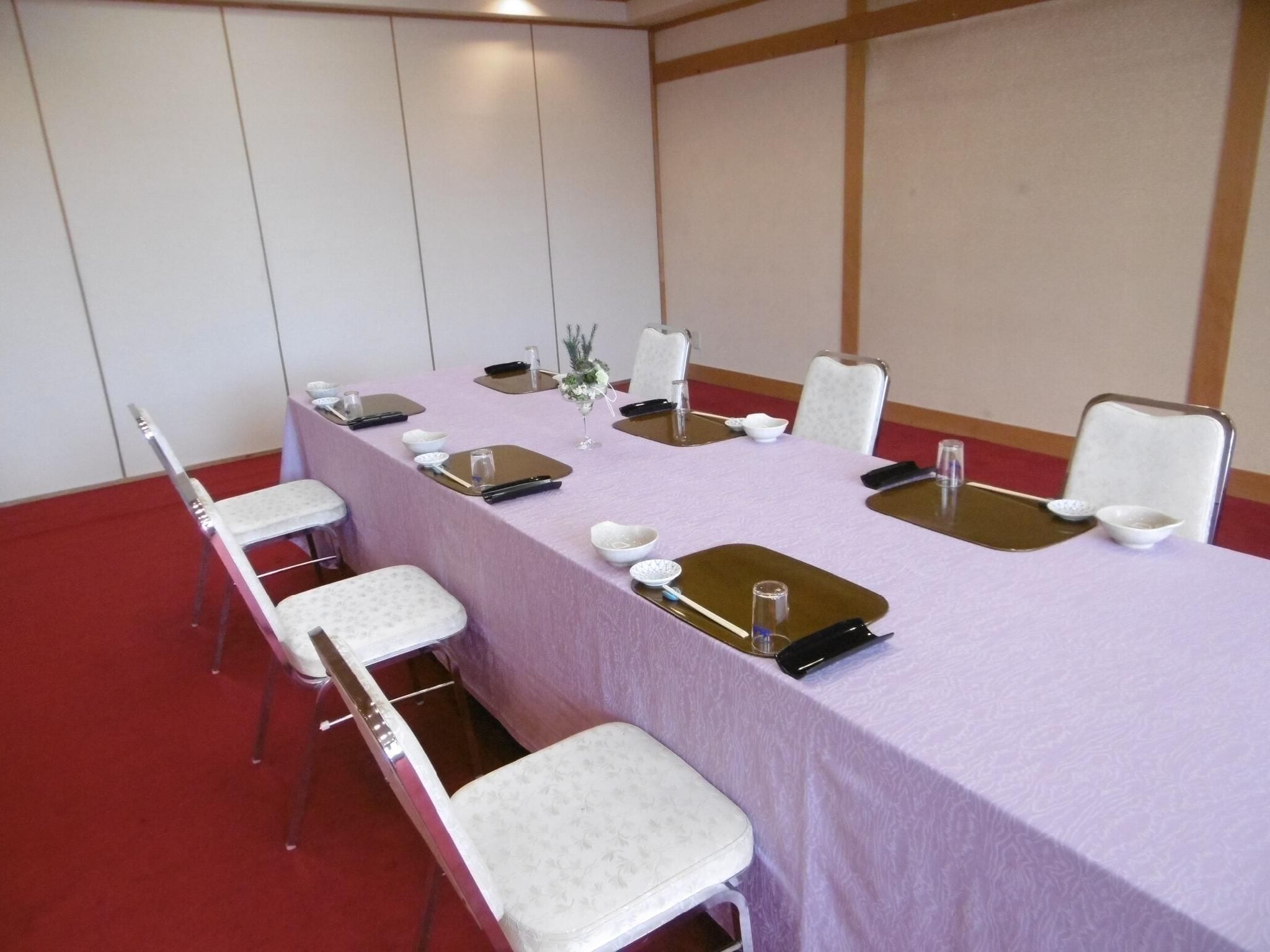 Uma sala de conferência com uma mesa comprida, cadeiras brancas e toalha de mesa roxa.