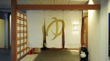 Um interior japonês tradicional com piso de tatame, um painel shoji com um símbolo dourado e uma estátua em preto e branco.