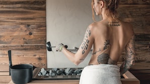 Uma pessoa tatuada em uma cozinha com parede de madeira e fogão moderno.