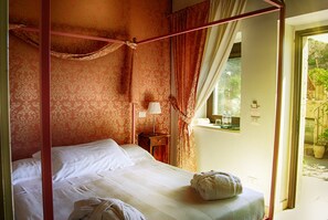 Quarto com cama de dossel, mesa de cabeceira com luminária e janela com vista para o verde.