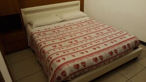 Cama com cabeceira branca e colcha estampada com corações.