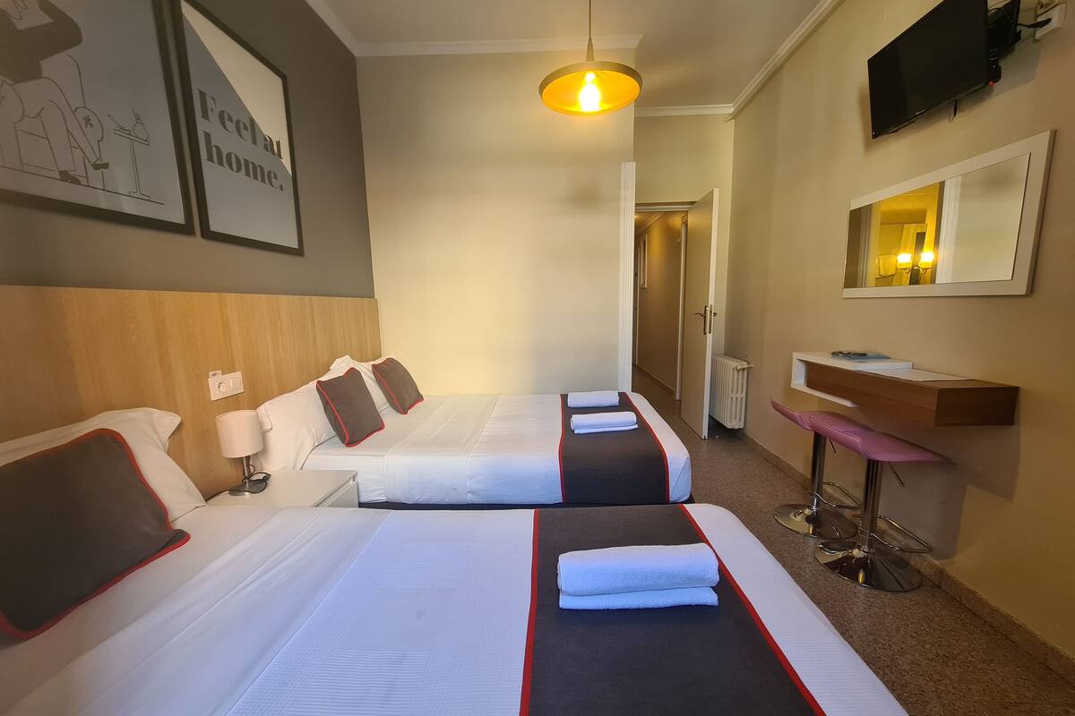 Quarto de hotel com duas camas, uma escrivaninha, uma cadeira, um espelho e uma televisão.