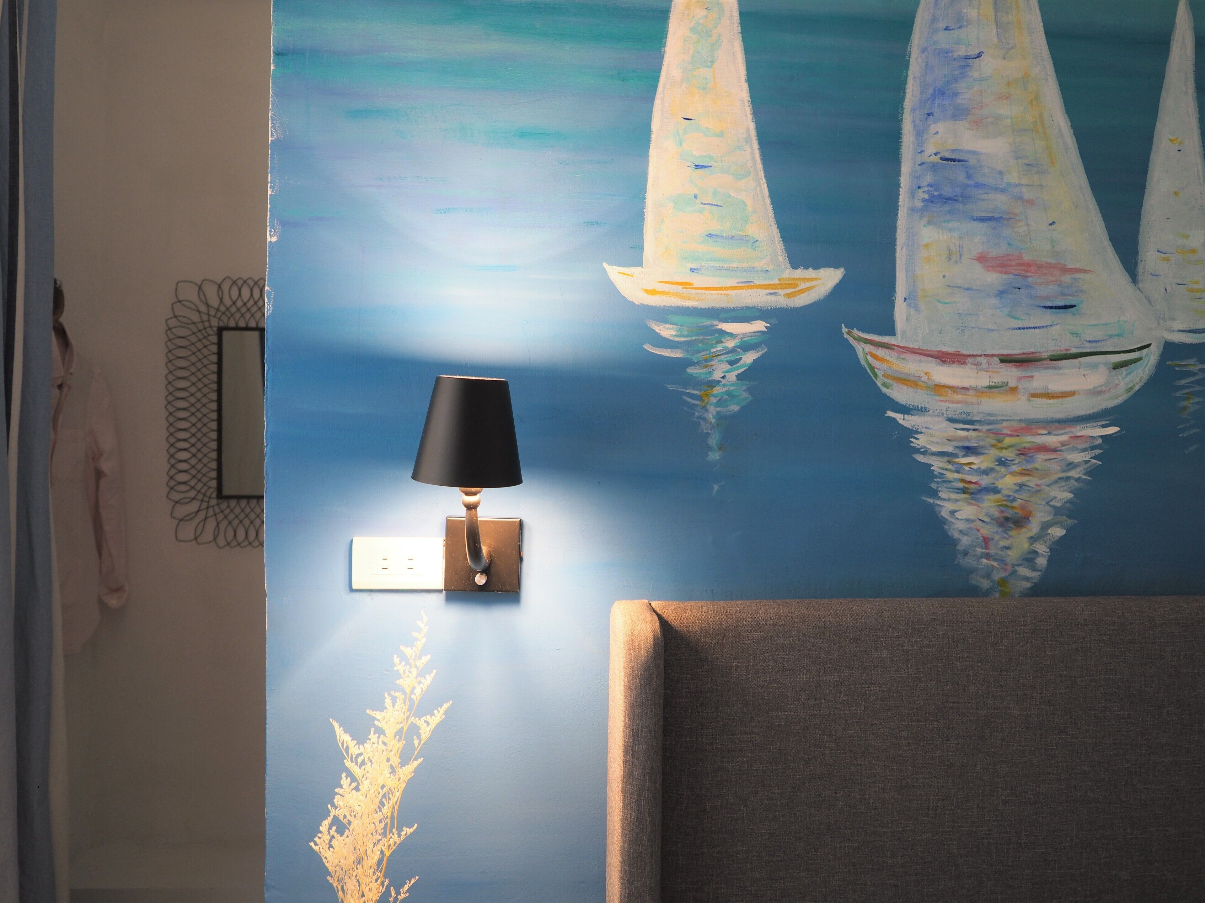 Parede com pintura de veleiros, luminária de parede e tomada.