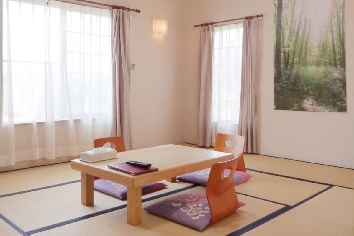 Um quarto japonês tradicional com tatames, uma mesa de madeira baixa, dois assentos de piso e um quadro na parede.