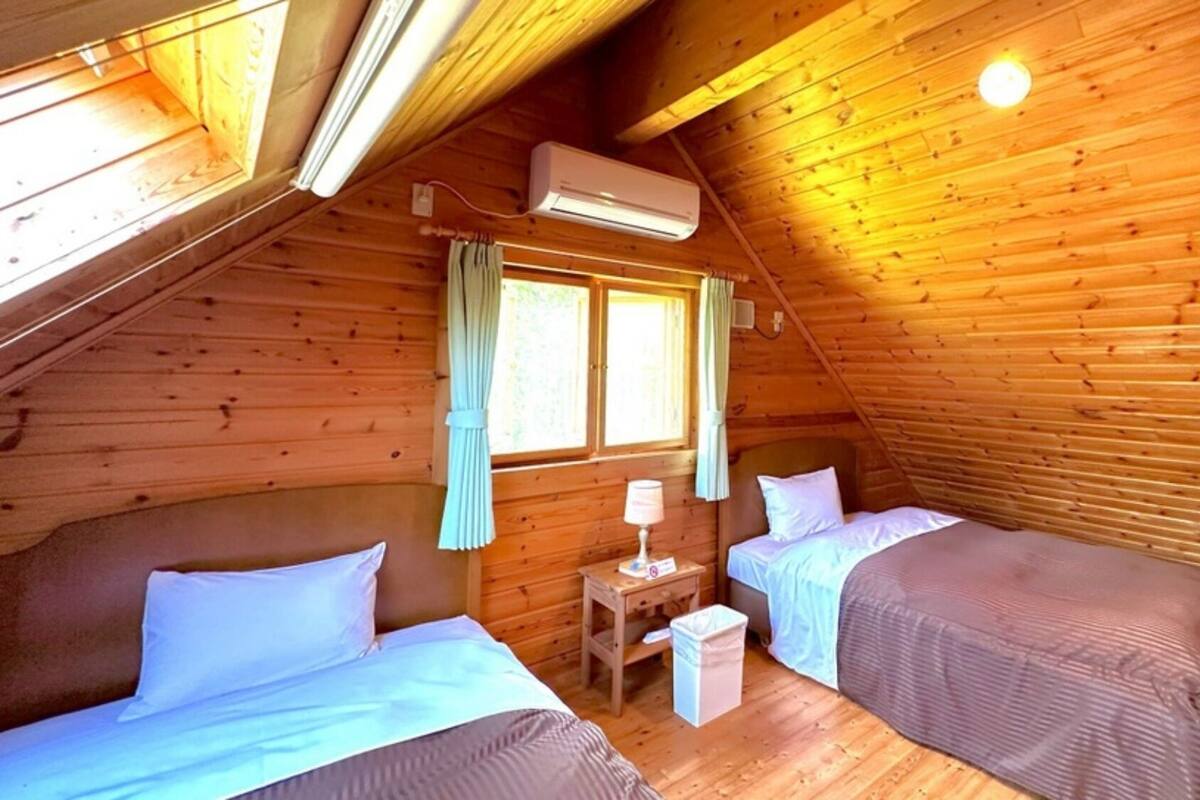Um quarto de sótão aconchegante com duas camas, uma mesinha e um ar condicionado.