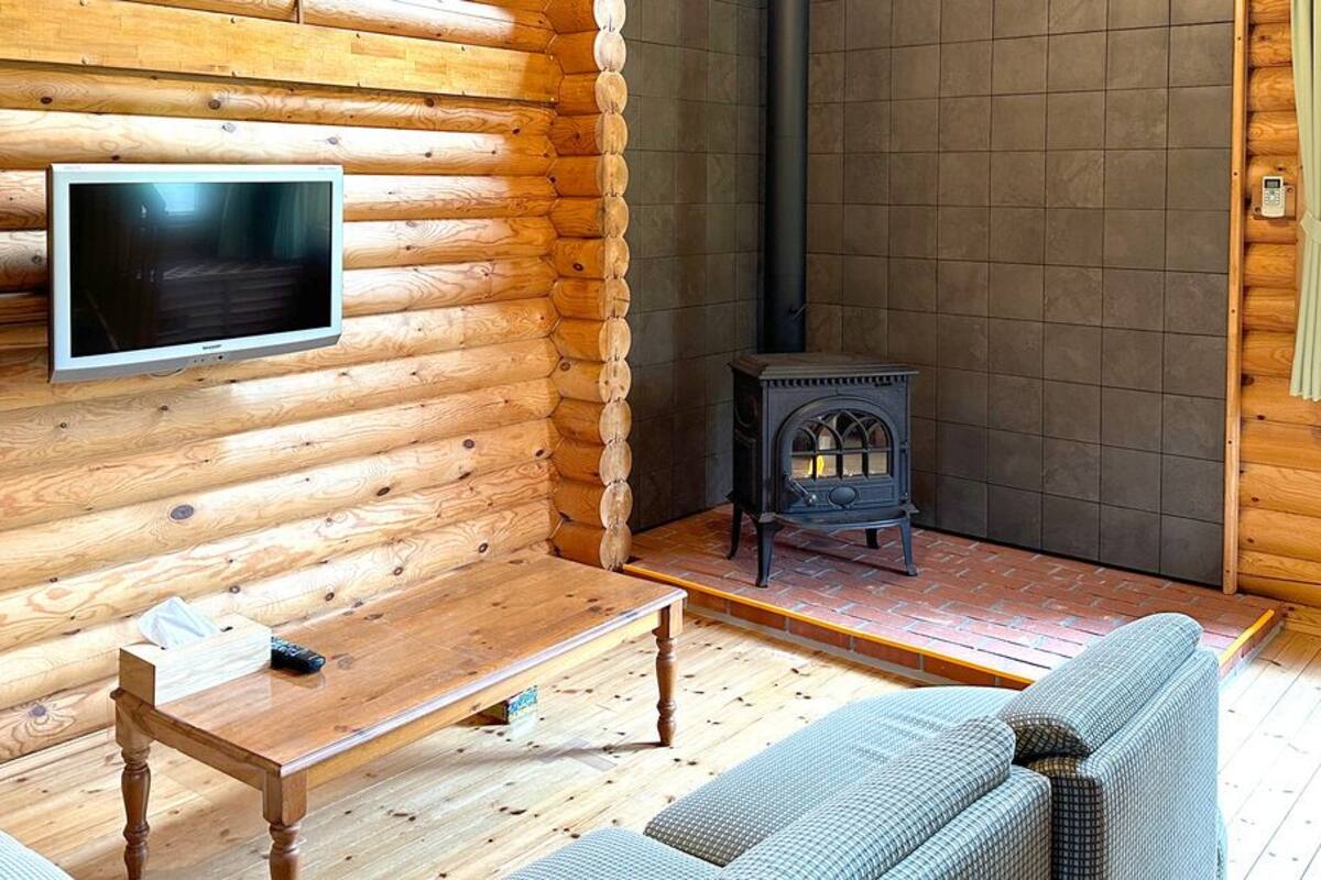 Interior de uma cabana de tronco com televisão, lareira, sofá e mesa de madeira.