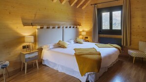 Quarto com painéis de madeira, uma cama grande, abajures, uma cadeira e uma janela com cortinas.