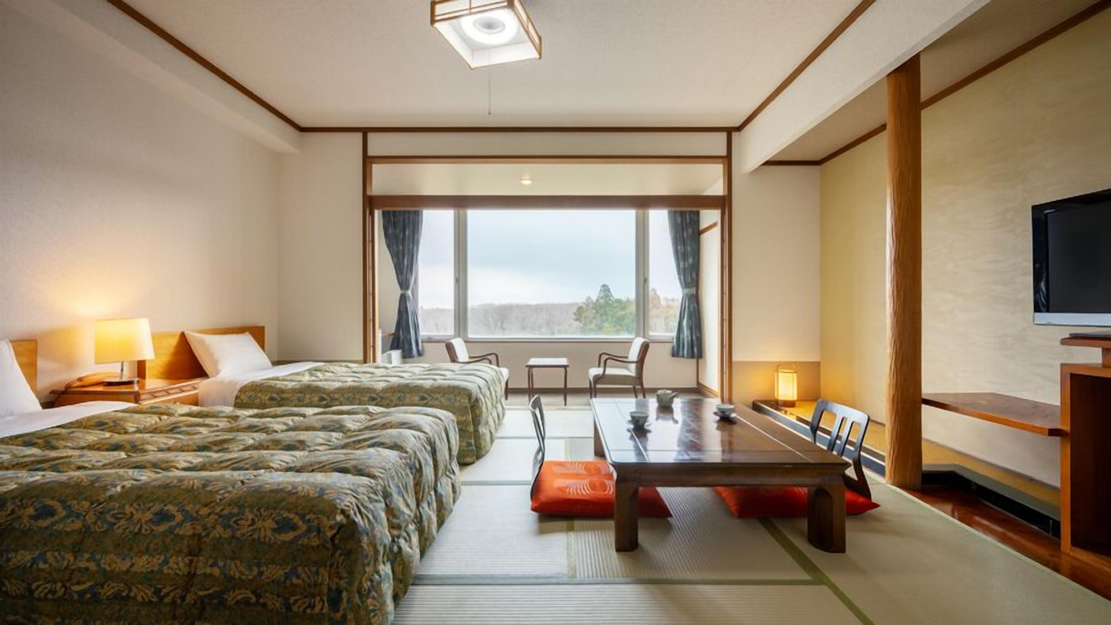 Quarto de hotel com duas camas, uma mesa de jantar, cadeiras, televisão e uma janela grande.
