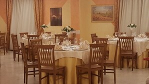 Uma área de refeições com mesas redondas, cadeiras de madeira e toalhas de mesa brancas.
