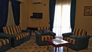 Uma sala de estar com sofás estampados, uma mesa de centro de madeira e uma televisão na parede.