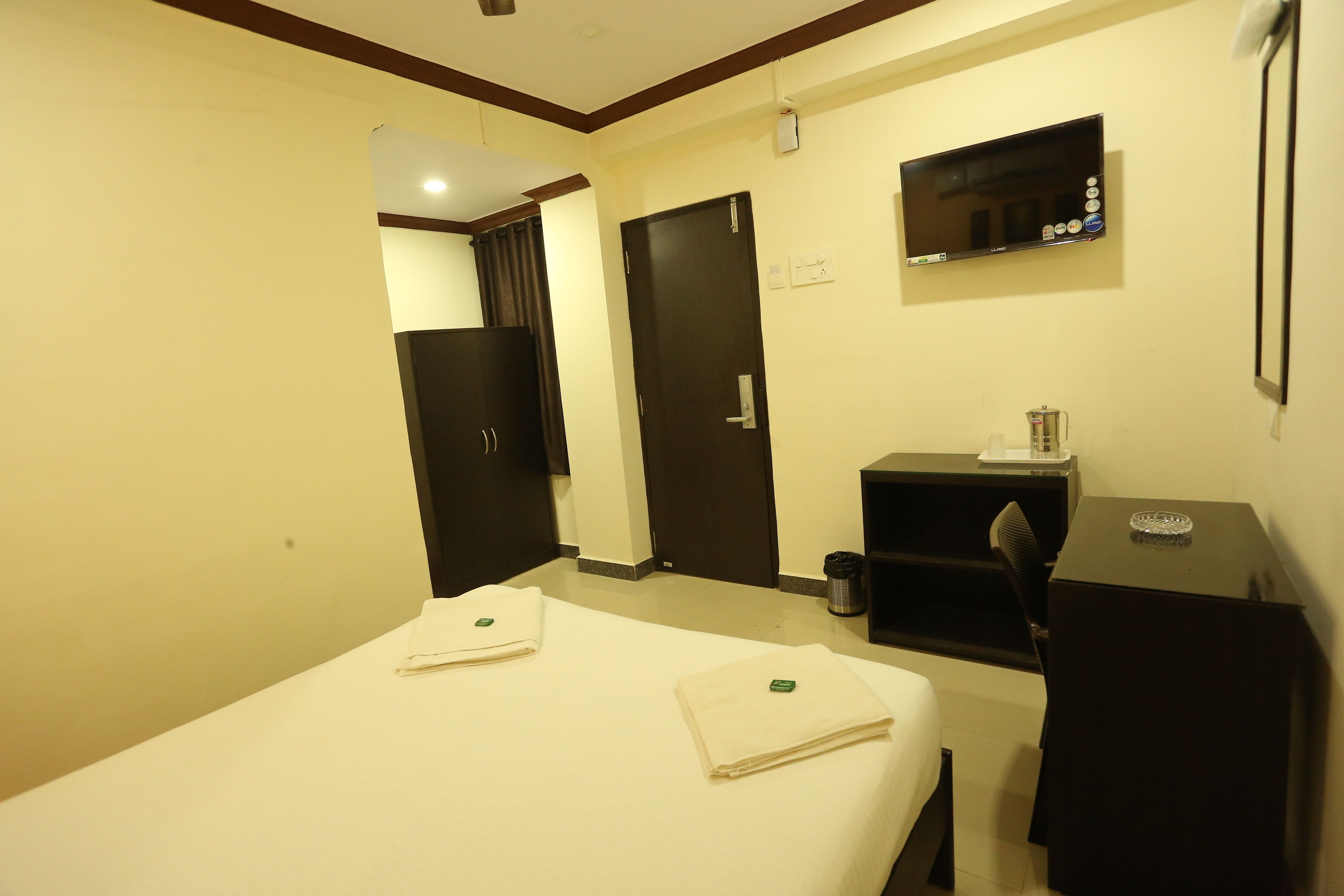 Quarto de hotel com cama, escrivaninha, televisão e porta.