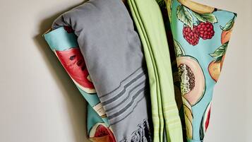 Uma bolsa colorida estampada com frutas, um travesseiro cinza e um cachecol verde.