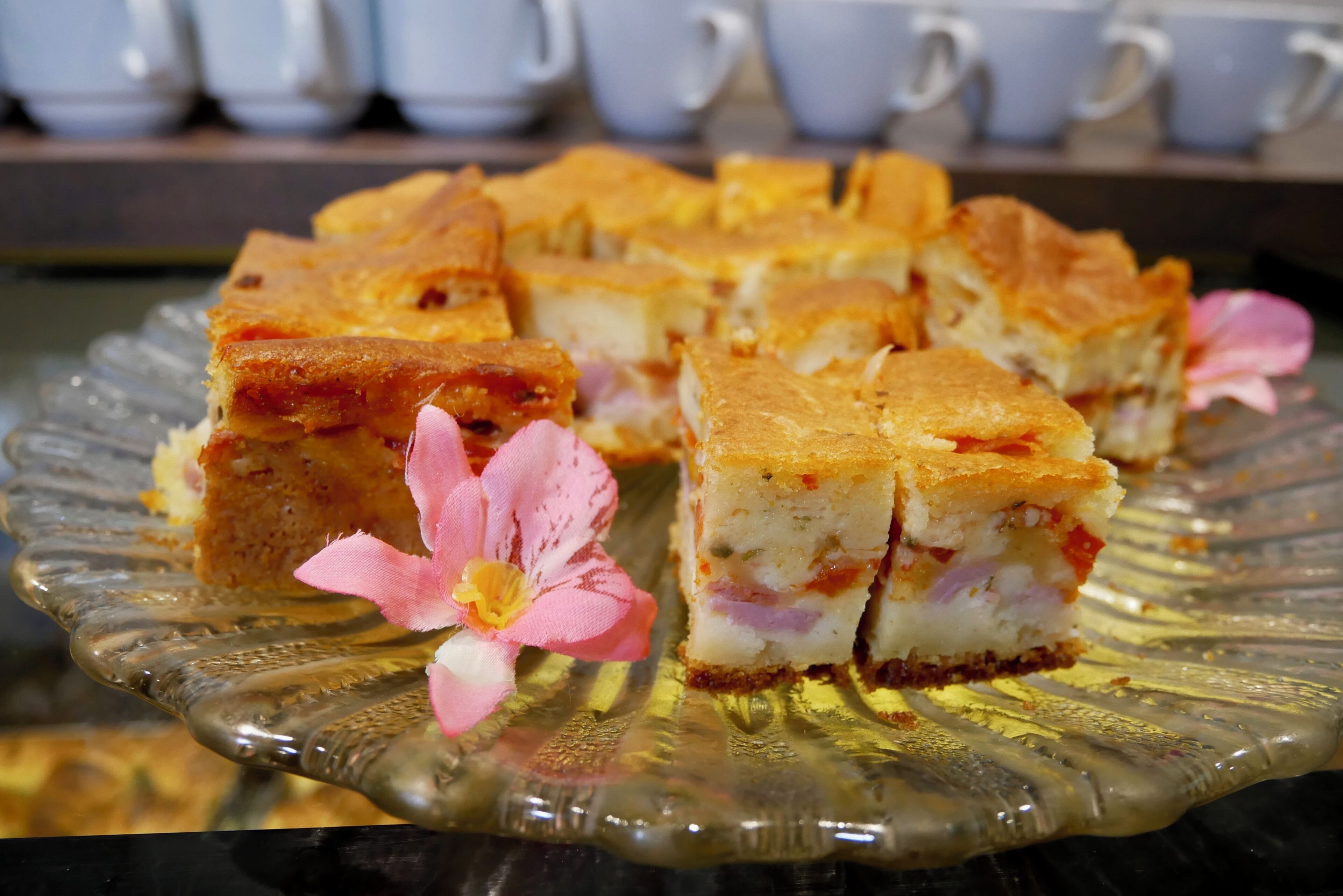 Um prato de vidro com uma fatia de bolo e uma flor rosa.