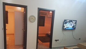 Quarto com televisão na parede, relógio e porta que dá para outro espaço.