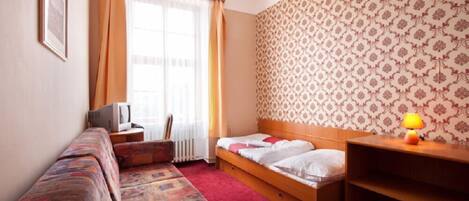 Quarto de hotel pequeno com cama, sofá, televisão e luminária.
