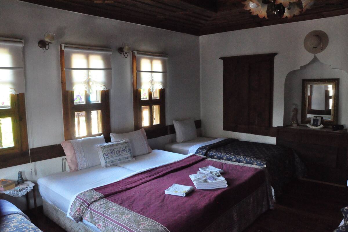 Quarto com duas camas, cômoda de madeira, espelho e janela com vista.