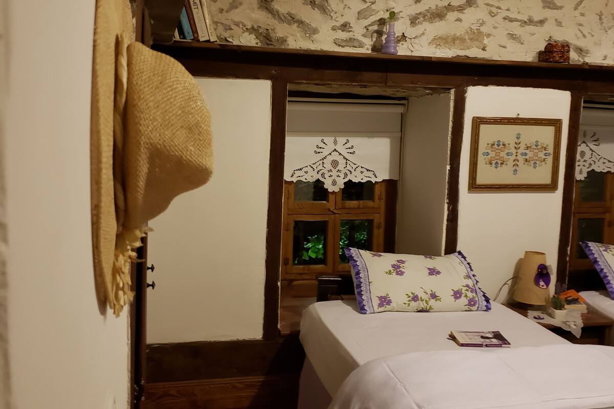 Quarto com piso de madeira, cama com roupa de cama branca, mesa de cabeceira com abajur e espelho na parede.