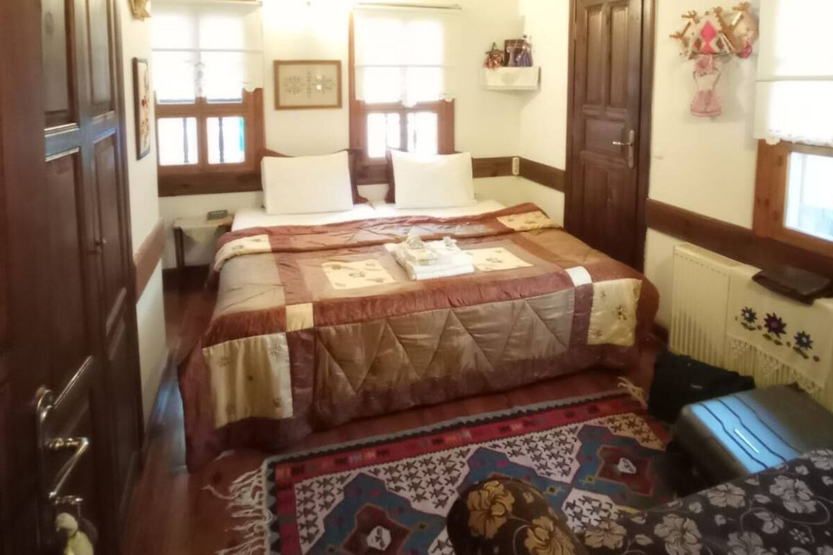 Quarto com teto de madeira, cama com colcha, radiador e janela com cortinas.