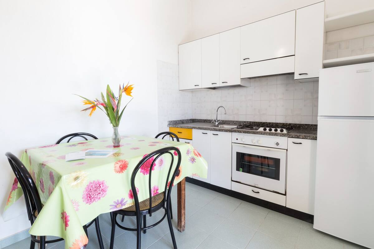 Uma cozinha com armários brancos, um fogão e uma mesa com toalha de mesa florida.