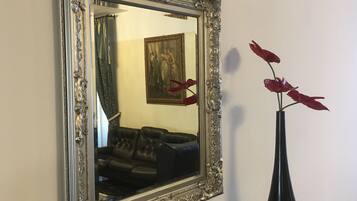 Espelho com moldura decorativa em uma parede, refletindo um quarto com sofá e pintura.