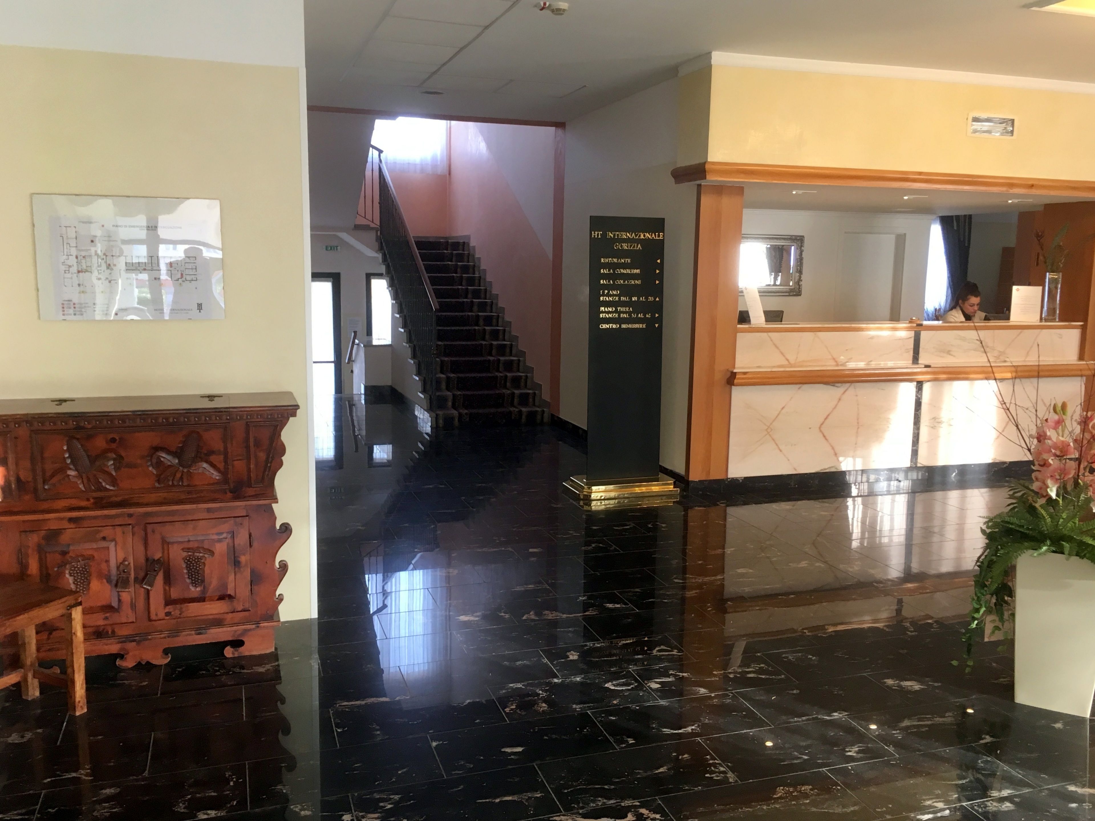 Um saguão de hotel com balcão de recepção, escada e um armário de madeira.