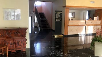 Um saguão de hotel com balcão de recepção, escada e um armário de madeira.
