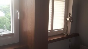 Quarto com janela, radiador, escrivaninha com luminária e uma cama.