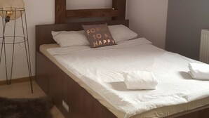 Quarto com estrutura de cama de madeira, cabeceira, abajur e tapete felpudo.