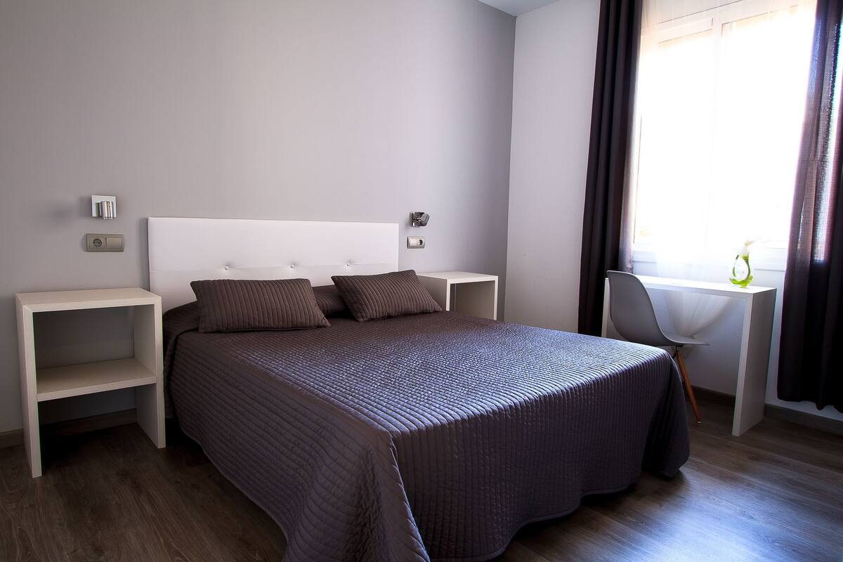 Quarto moderno com uma cama grande, duas mesas de cabeceira, uma escrivaninha e uma cadeira.