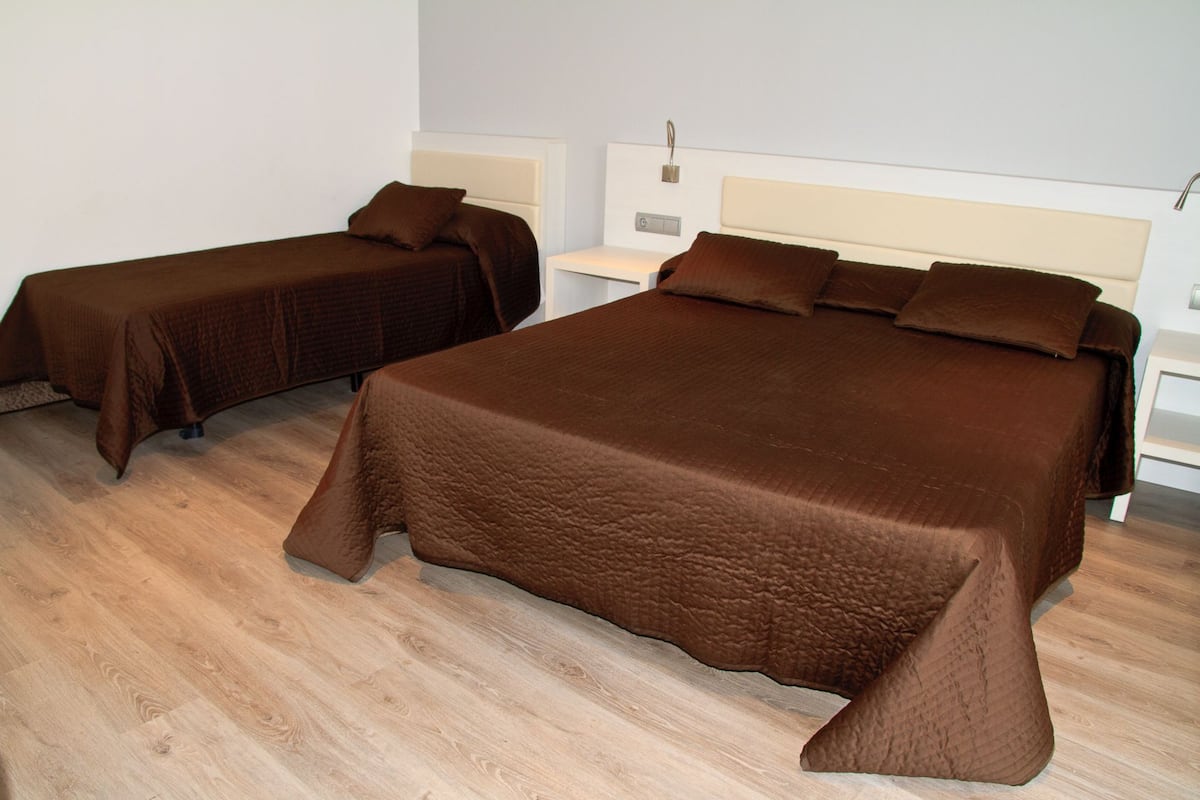 Duas camas com roupa de cama marrom num quarto com soalho de madeira e paredes brancas.