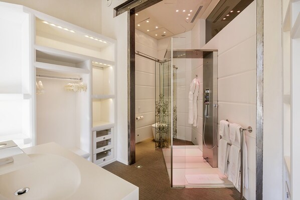 Um banheiro moderno com uma banheira grande e branca, chuveiro com box de vidro e um closet espaçoso com prateleiras.