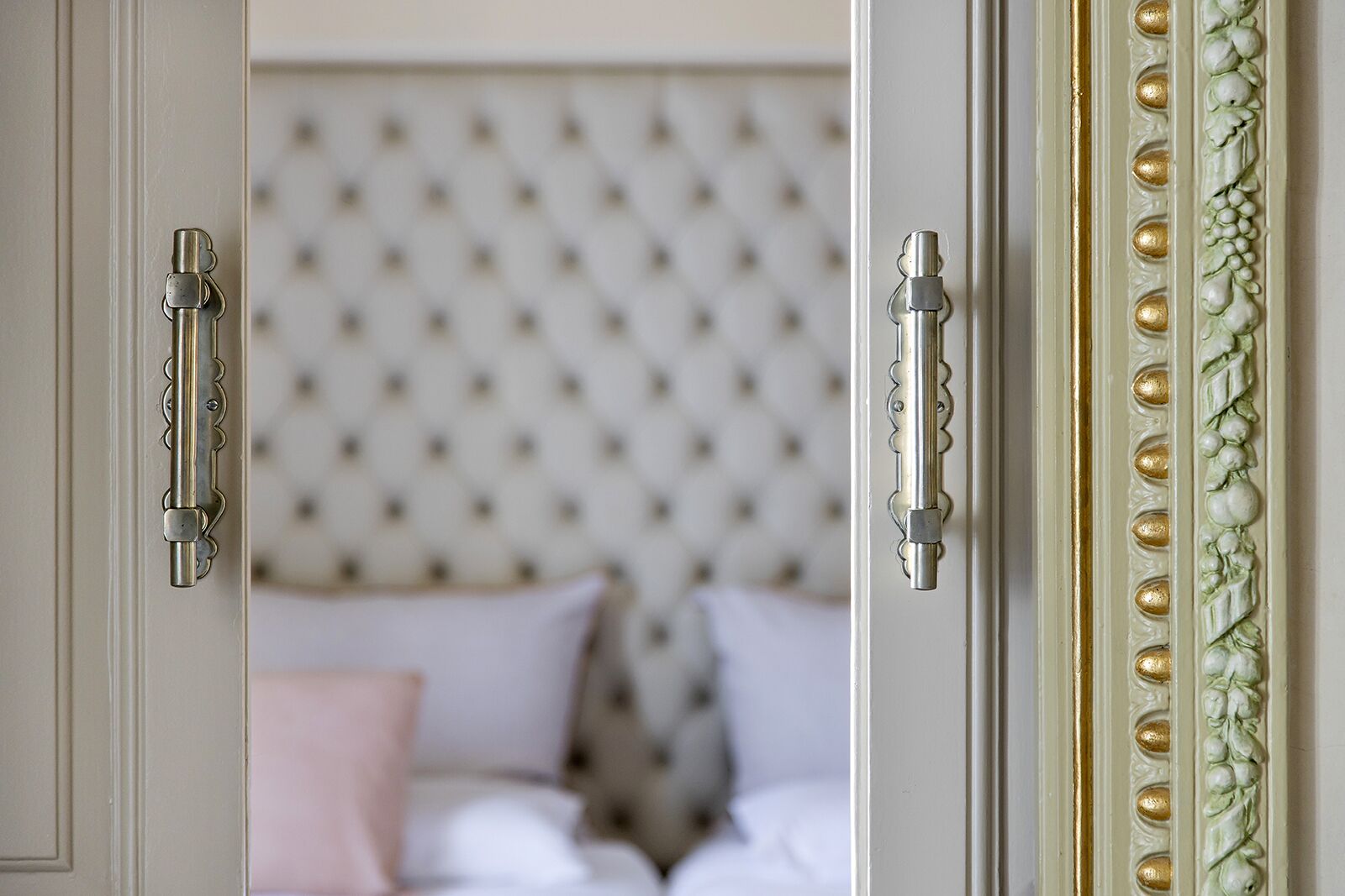 Quarto com cabeceira estofada, cama com roupa de cama branca e painel decorativo na parede.