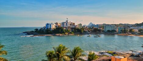 Paisagem costeira urbana com edifícios ao longo da praia, céu claro e mar calmo.