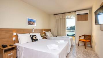 Quarto de hotel com duas camas, uma mesinha de cabeceira de madeira, uma cadeira e uma janela grande com cortinas.