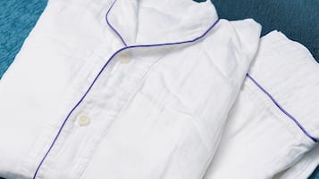 Uma camisa branca bem dobrada, com detalhes em azul e botões, apoiada em uma superfície azul com textura.