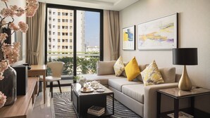 Quarto de hotel moderno com sofá, mesa de centro e vista para um edifício alto.