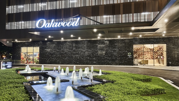 Entrada de um hotel com um espelho d'água e uma placa com o nome 'Oakwood'.