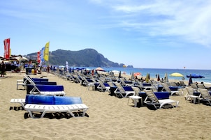 Uma praia com fileiras de espreguiçadeiras azuis e brancas, bandeiras e guarda-sóis.