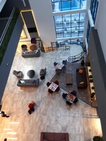 Espaço interno com teto alto, área de estar central com sofás e cadeiras, e vista para o exterior através de amplas janelas.
