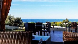 Um pátio externo com móveis de vime e vista para o mar.
