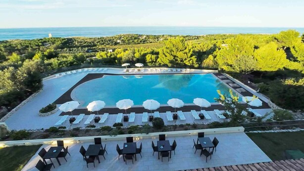 Resort com uma grande piscina cercada por espreguiçadeiras e guarda-sóis, com vista para a área costeira.