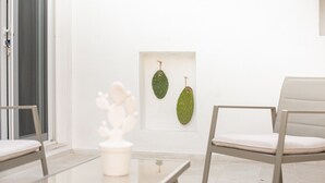Sala de estar minimalista com uma mesa de centro de vidro, um sofá branco e duas folhas decorativas verdes na parede.