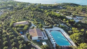 Vista aérea de uma área residencial com piscina, rodeada por vegetação densa e alguns edifícios.