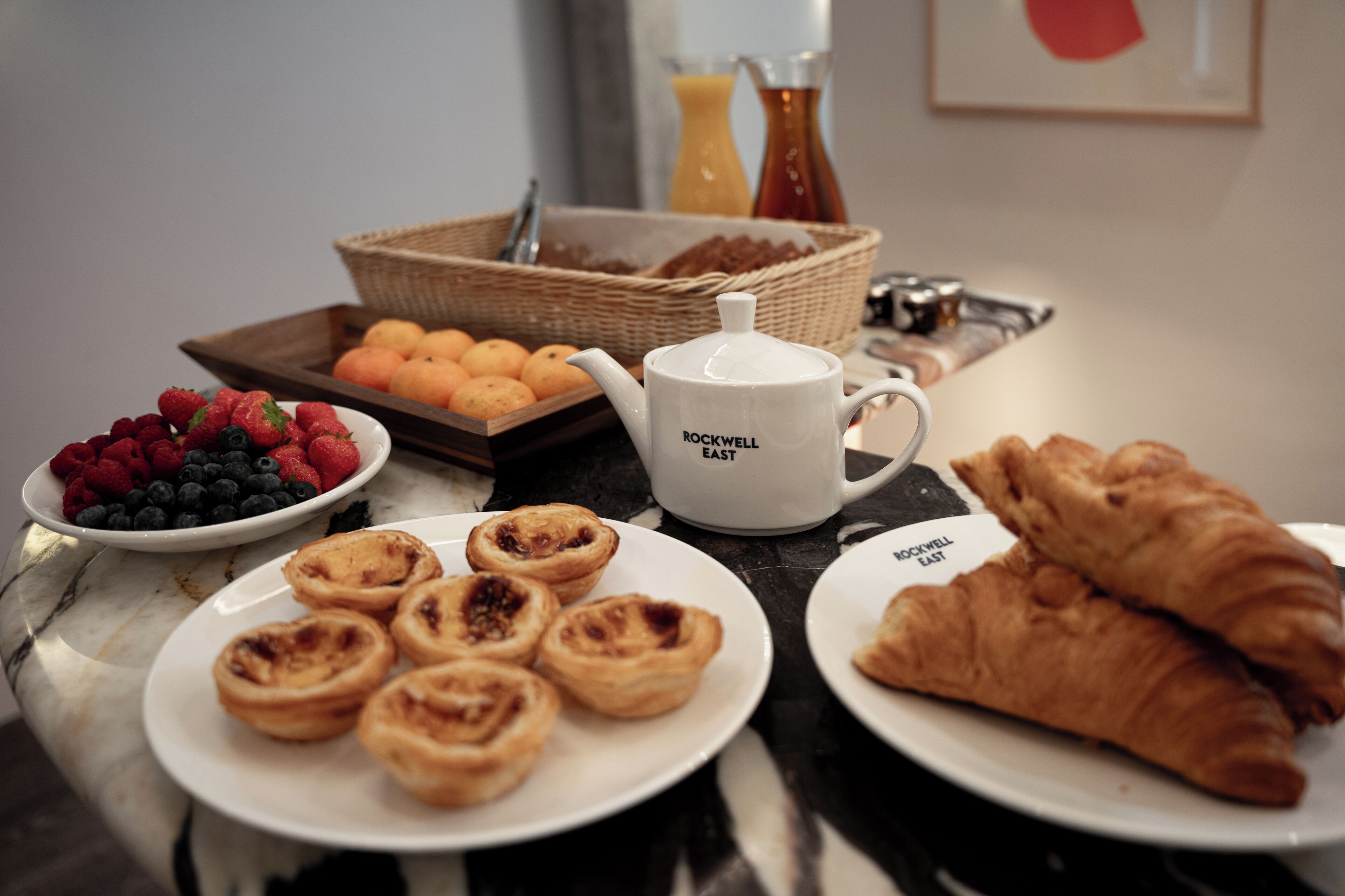 Uma mesa de café da manhã com doces, frutas e uma cafeteira.