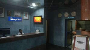 Uma área de recepção com balcão, tela de televisão, certificados emoldurados e um relógio na parede.