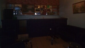 Um bar com iluminação fraca, parede de tijolos, prateleiras cheias de garrafas e um quadro na parede.