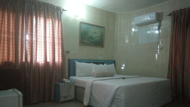 Quarto de hotel com cama, mesa de cabeceira, telefone e aparelho de ar condicionado.
