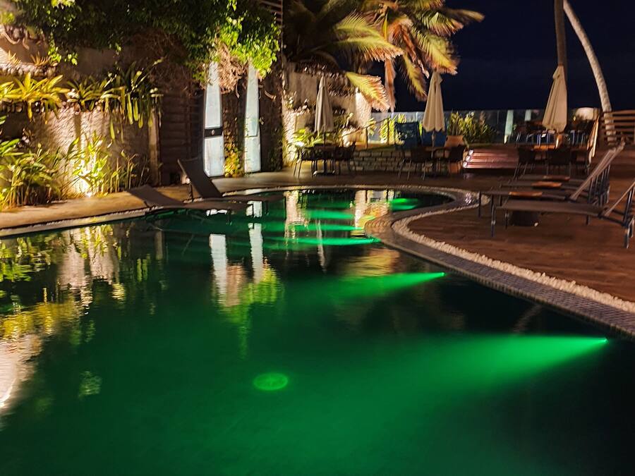 Uma área de piscina à noite, com espreguiçadeiras e palmeiras.