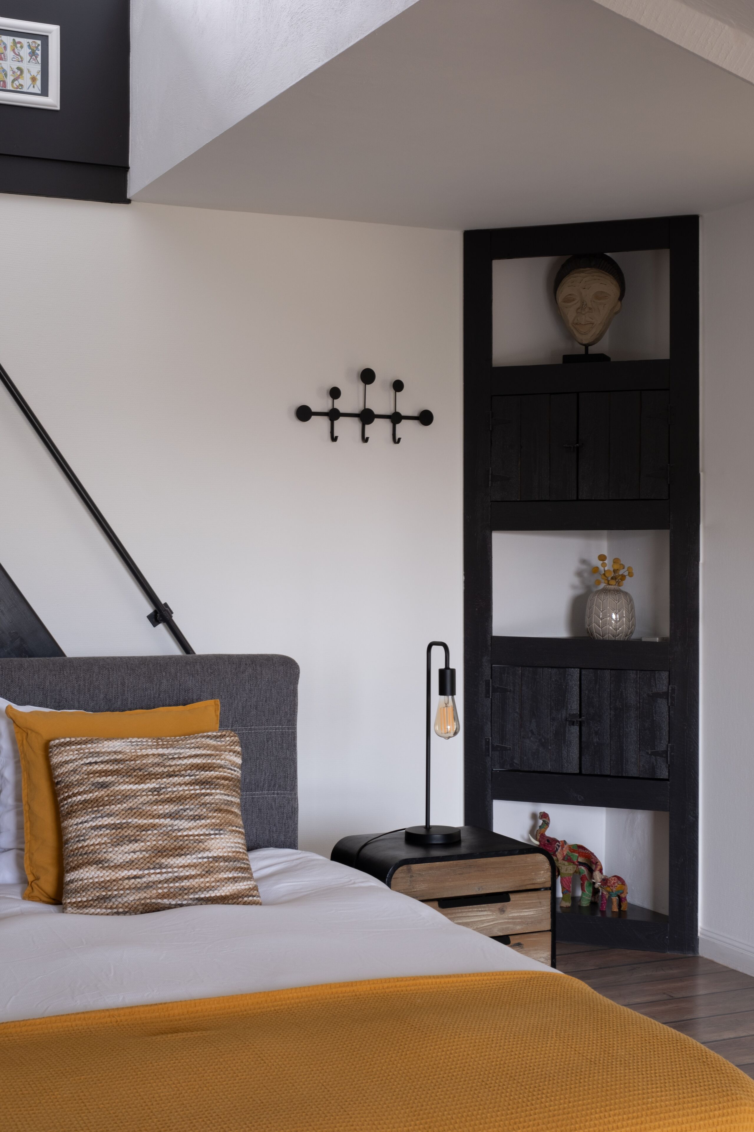 Quarto moderno com cama, mesa de cabeceira, luminária de parede e prateleira decorativa com um vaso e figuras.